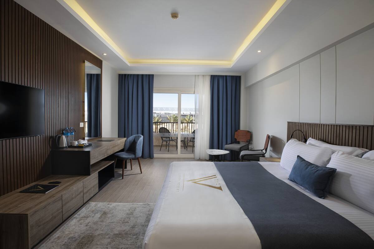 Quarto de hotel moderno com uma cama grande, uma escrivaninha, televisão e varanda com vista.