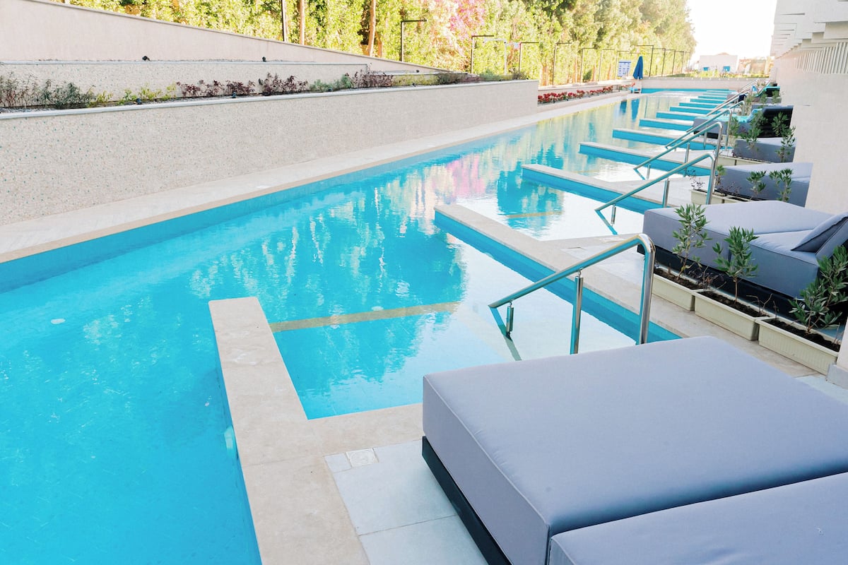 Piscina com degraus de acesso, cercada por espreguiçadeiras e um muro baixo com plantas.