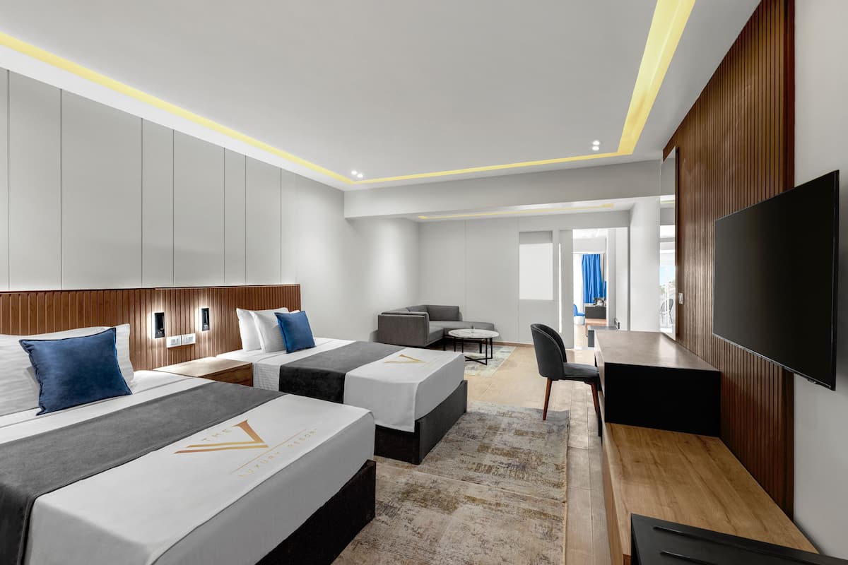 Quarto de hotel moderno com três camas, uma escrivaninha, uma TV e vista para a cidade.