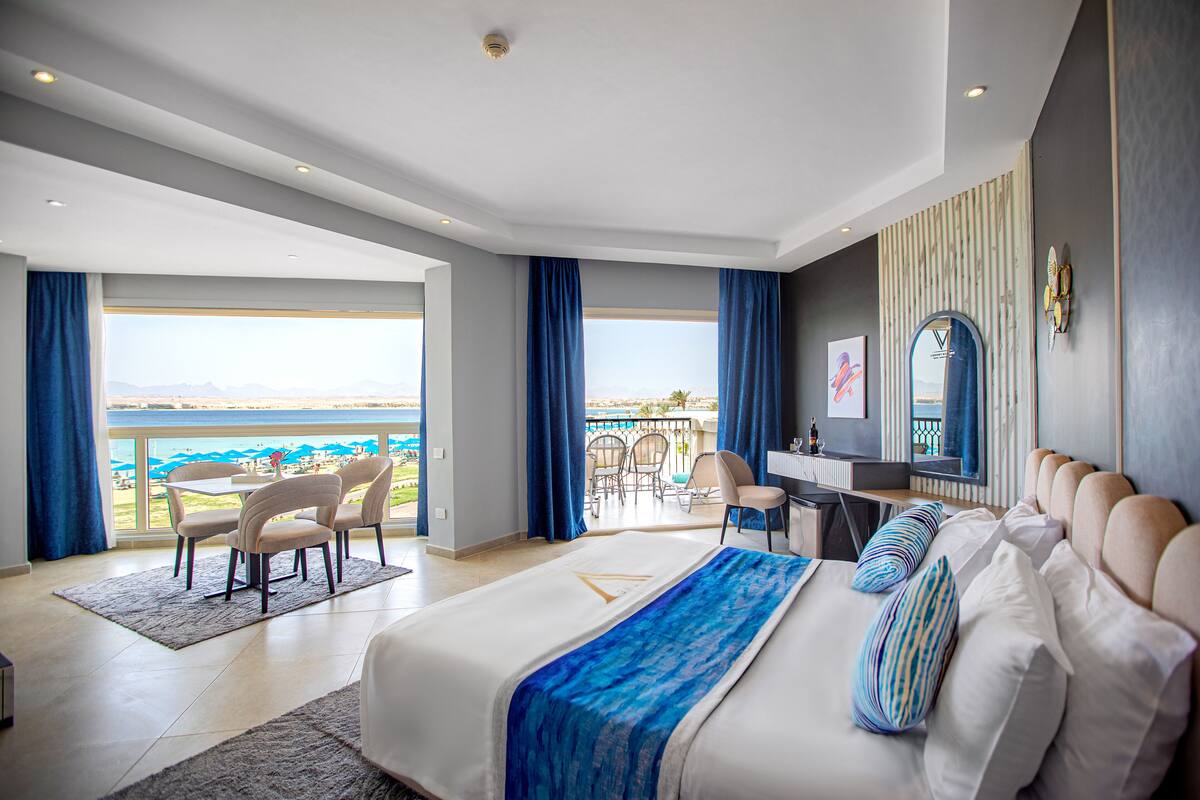 Quarto de hotel com uma cama grande, uma escrivaninha e uma varanda com vista para o mar.