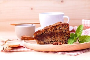 Uma fatia de bolo de frutas sobre uma tábua de madeira, uma xícara branca e uma folha de hortelã.