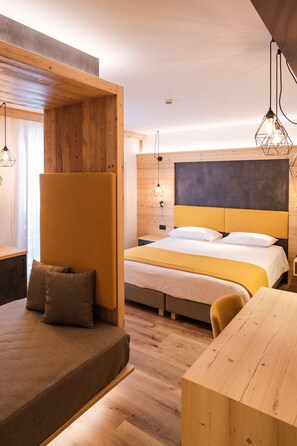 Quarto moderno com cabeceira de madeira, cama com roupa de cama branca, escrivaninha de madeira e um sofá.