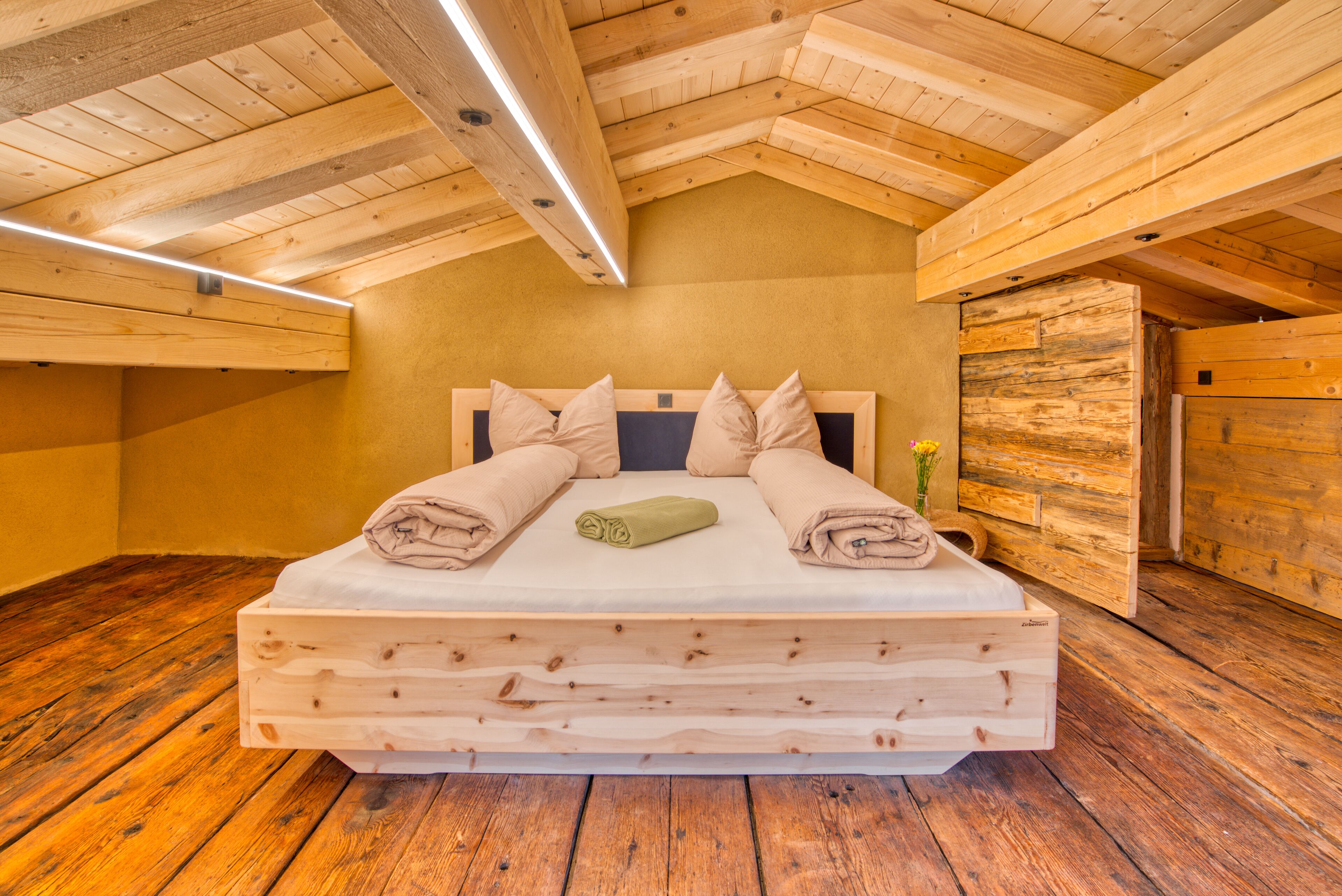 Uma cama de madeira num quarto com teto inclinado e paredes de madeira.