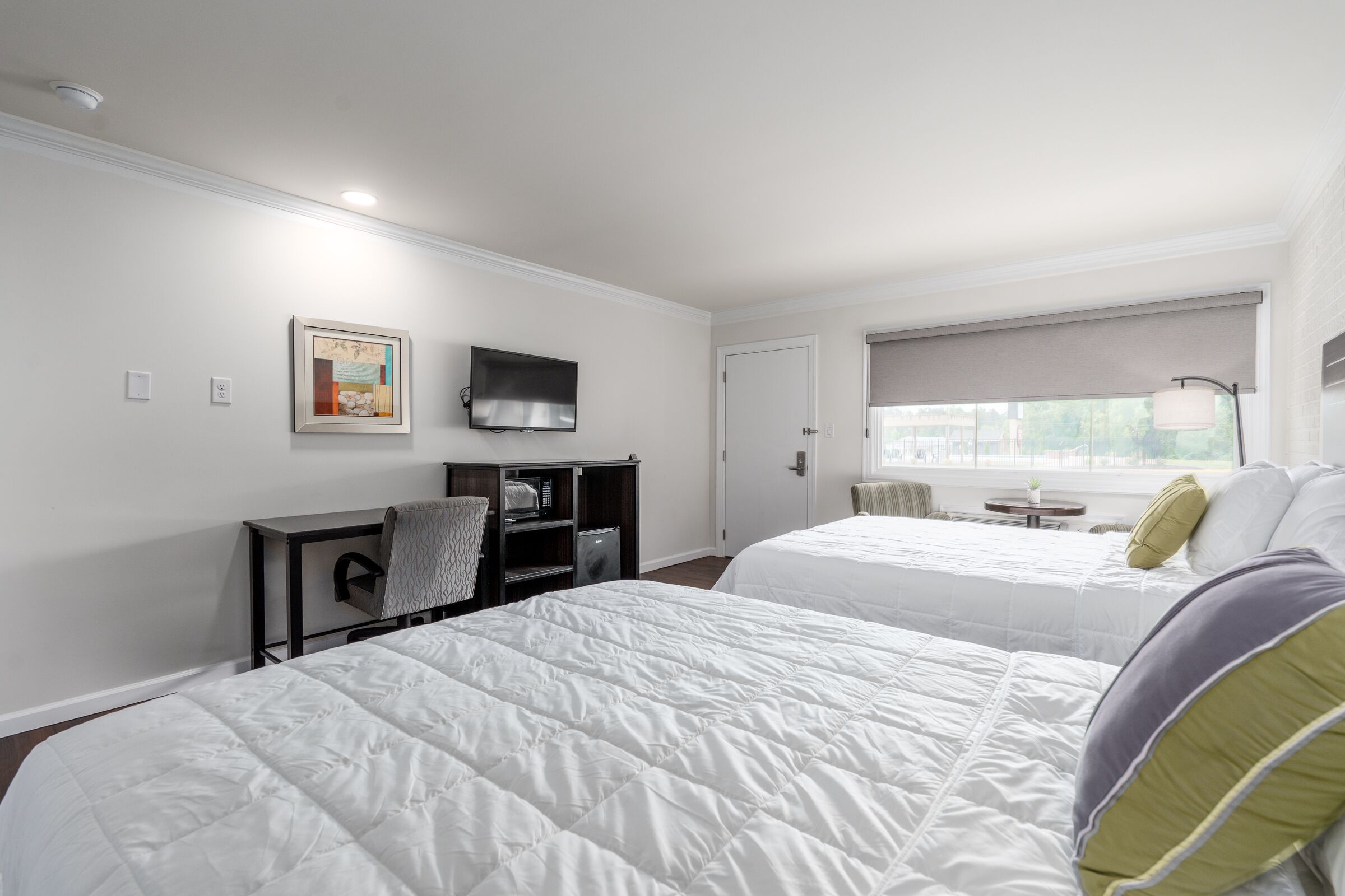 Quarto de hotel com duas camas, uma mesa com cadeira, televisão e janela com vista.