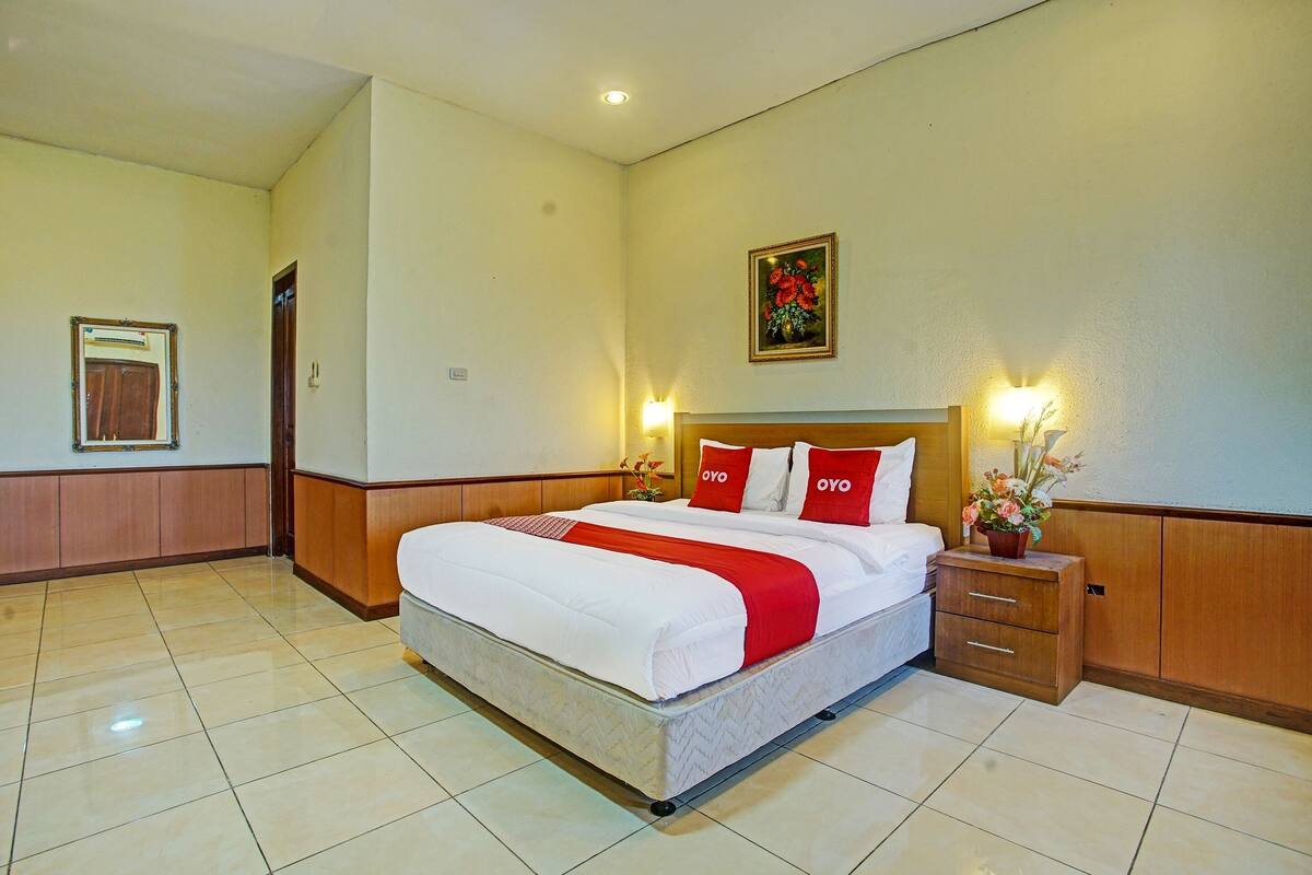Quarto de hotel com cama grande, cabeceira de madeira, mesas de cabeceira com luminárias e um quadro na parede.