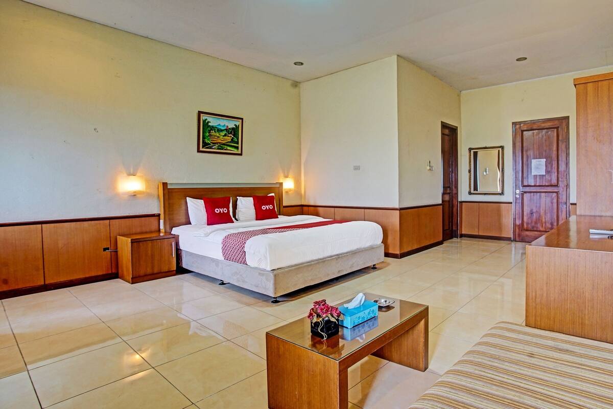 Quarto de hotel com uma cama, mesas de cabeceira, uma mesinha de centro, um sofá e um guarda-roupa de madeira.
