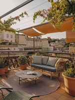 Terraço no telhado com sofá, mesa redonda e plantas em vasos.