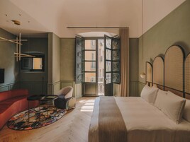 Quarto de hotel moderno com uma cama grande, um sofá vermelho, uma mesa redonda pequena e um tapete colorido.