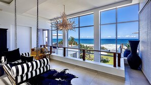 Uma sala de estar moderna com uma grande janela com vista para o oceano, um lustre pendurado e um sofá listrado em preto e branco.