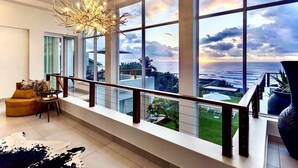 Um interior moderno com grandes janelas que oferecem vista para o oceano e uma varanda com guarda-corpo.