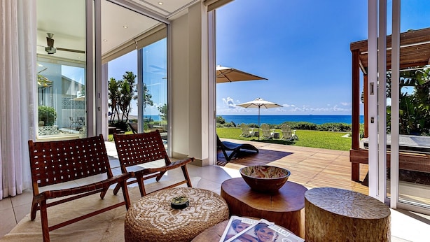Varanda ampla vista para o mar, móveis de madeira e porta de vidro que dá para o interior.