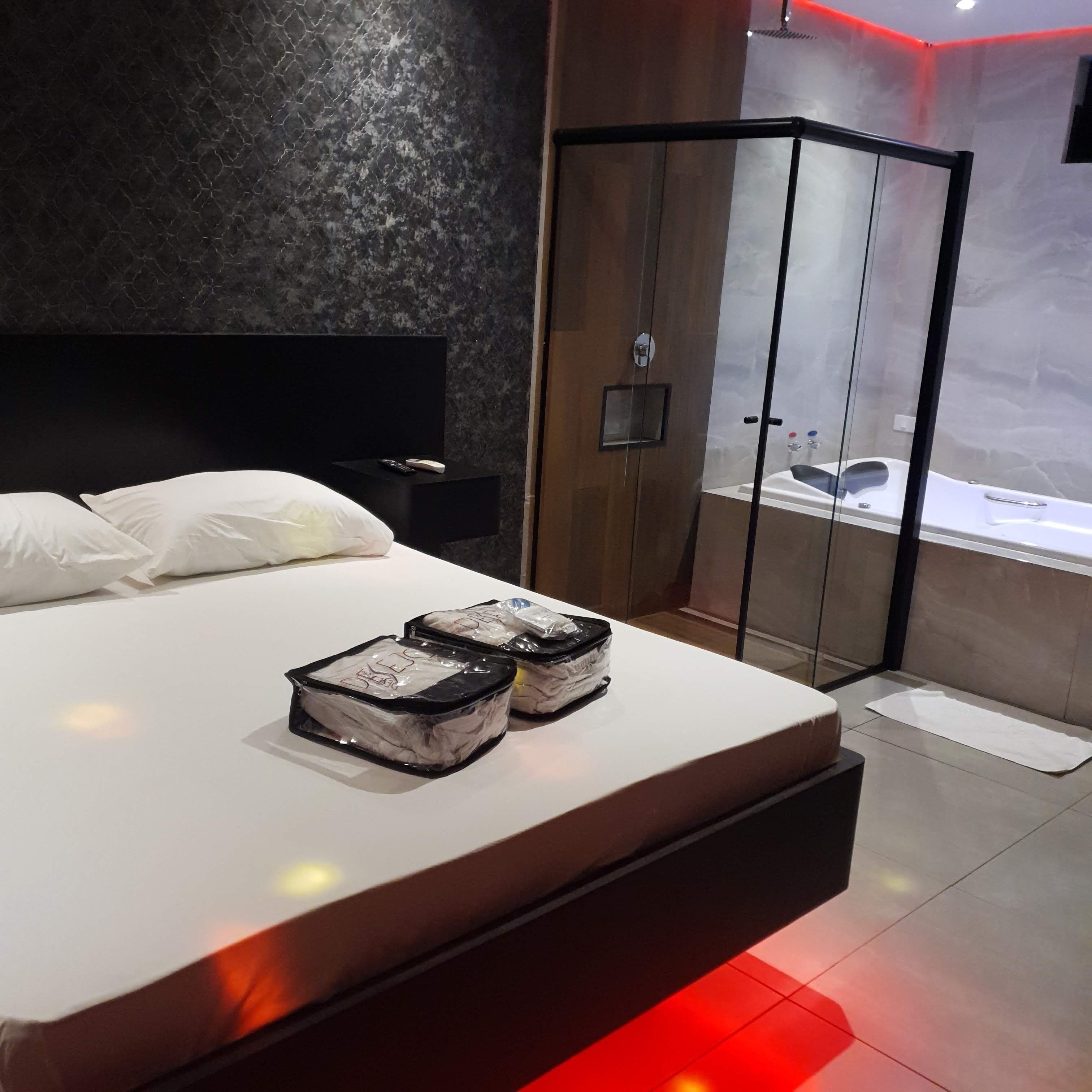 Quarto de hotel moderno com uma cama grande, chuveiro em cabine de vidro e parede escura com textura.
