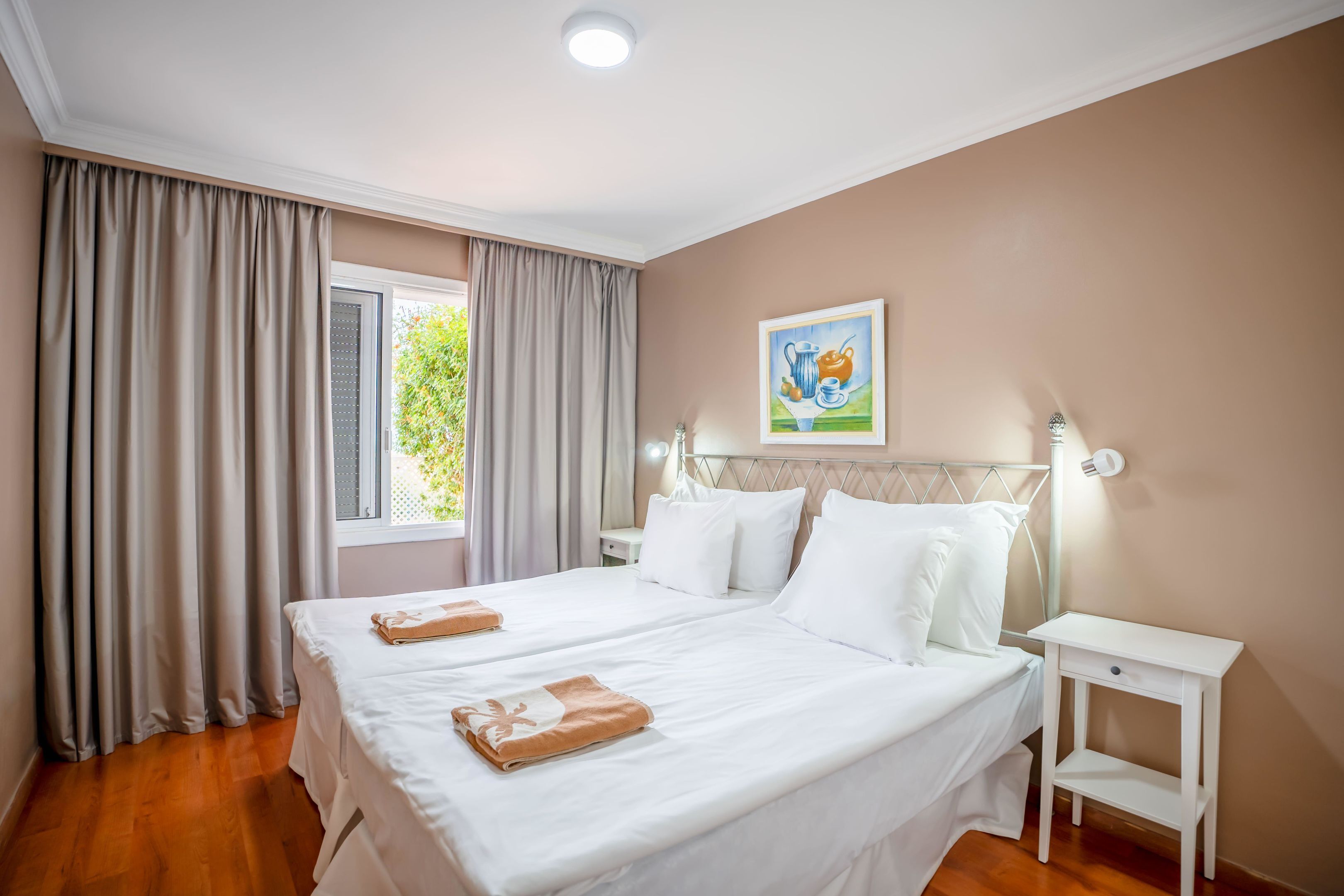 Quarto de hotel com uma cama grande, uma mesa de cabeceira, cortinas em uma janela e um quadro na parede.