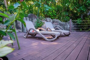 Um deck de madeira com três cadeiras de descanso e uma parede de pedra.