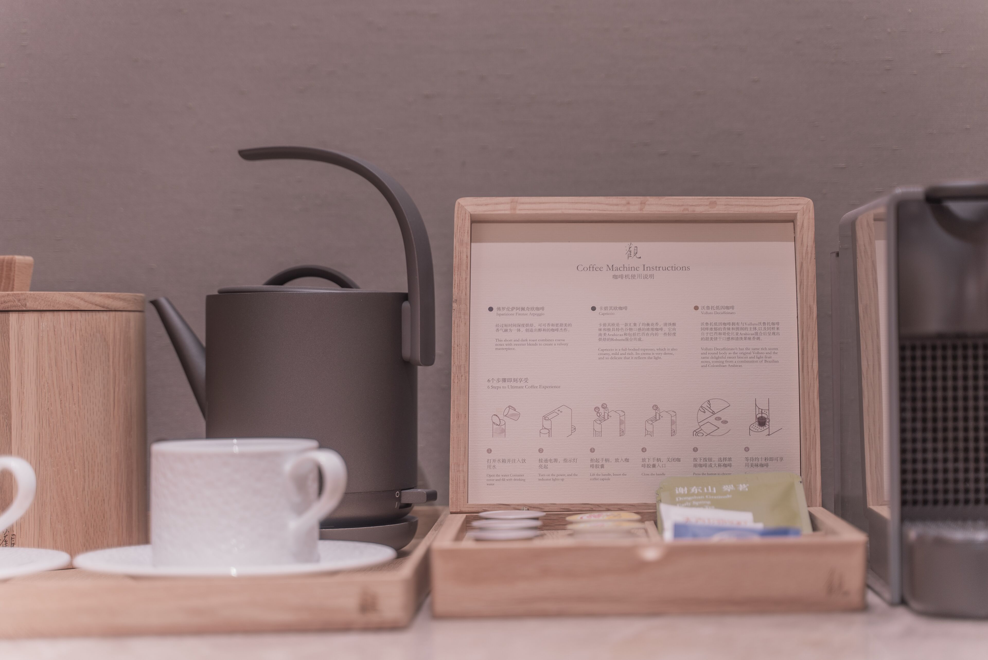 Máquina de café com manual, uma chávena e um tabuleiro com cápsulas de café.