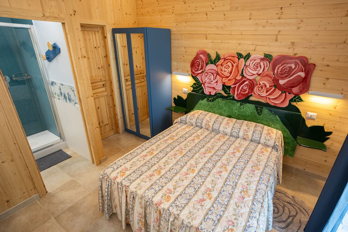 Quarto com cama, chuveiro e parede de madeira com um mural floral.