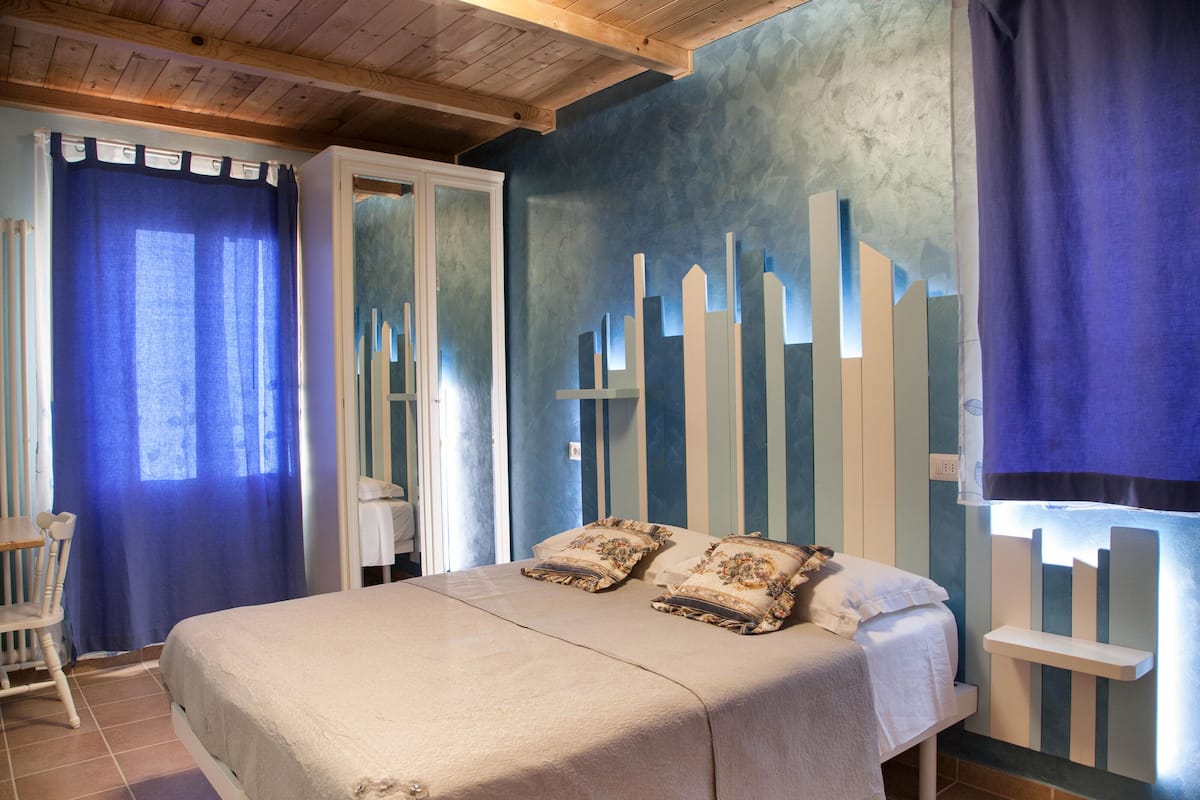 Quarto com cama, uma cadeira, cômoda e parede com ripas de madeira verticais.