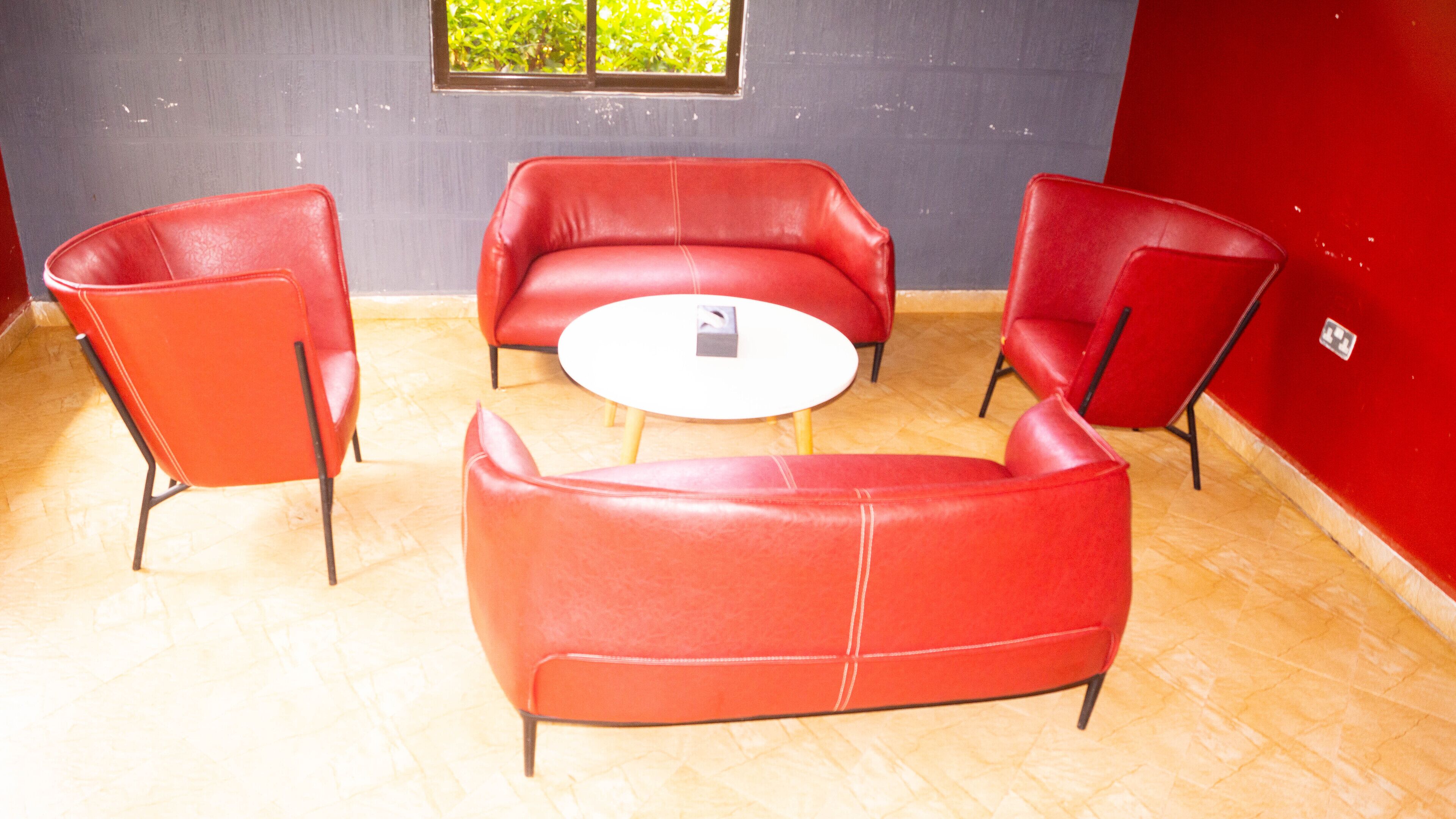 Quarto com um sofá vermelho, duas poltronas vermelhas e uma pequena mesa branca.
