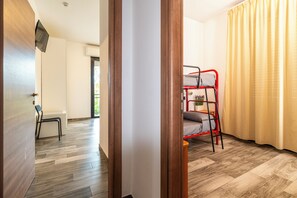 Quarto com beliche, uma cadeira, televisão presa na parede e porta que dá para outro cômodo.