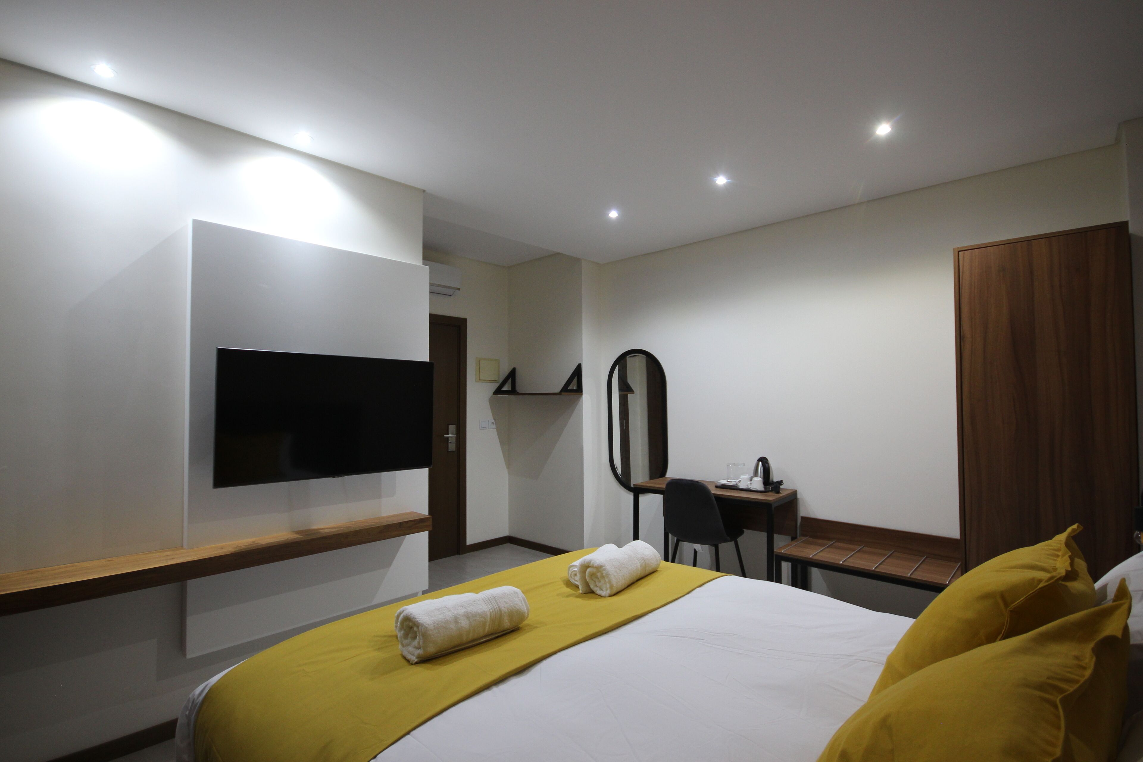 Quarto de hotel com cama, escrivaninha, cadeira, televisão na parede e guarda-roupa.
