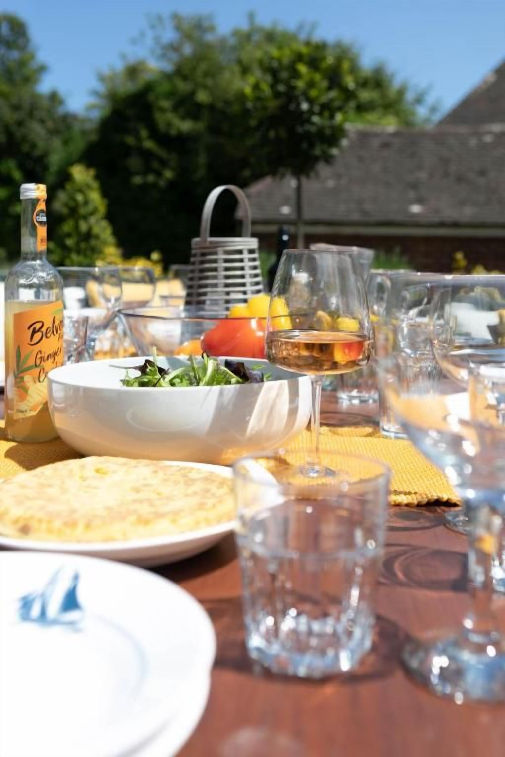 Mesa posta ao ar livre com uma garrafa de Bena Ginger Ale, uma saladeira e um copo de vinho.