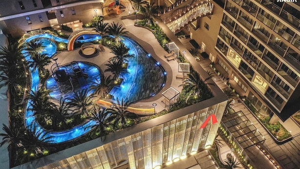 Vista aérea de um hotel com piscina, palmeiras e fachada de edifício moderna.