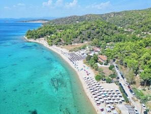 Uma área costeira com praia, águas turquesa cristalinas e uma fileira de carros estacionados à beira-mar.
