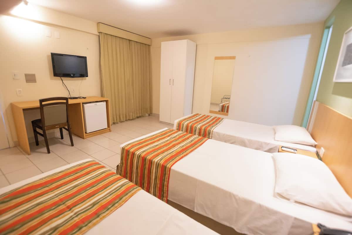 Quarto de hotel com três camas, uma mesa, uma televisão e um guarda-roupa.