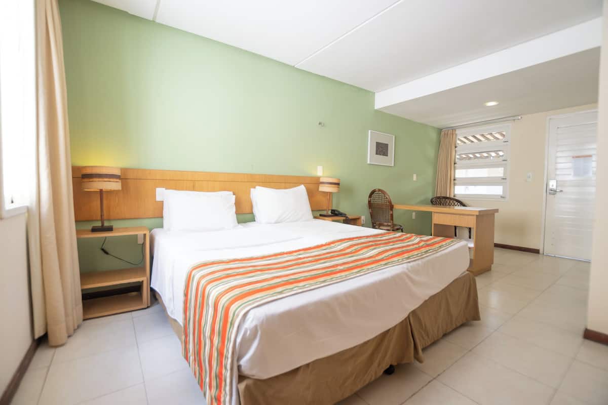 Quarto de hotel com cama, mesas de cabeceira, escrivaninha e uma cadeira.
