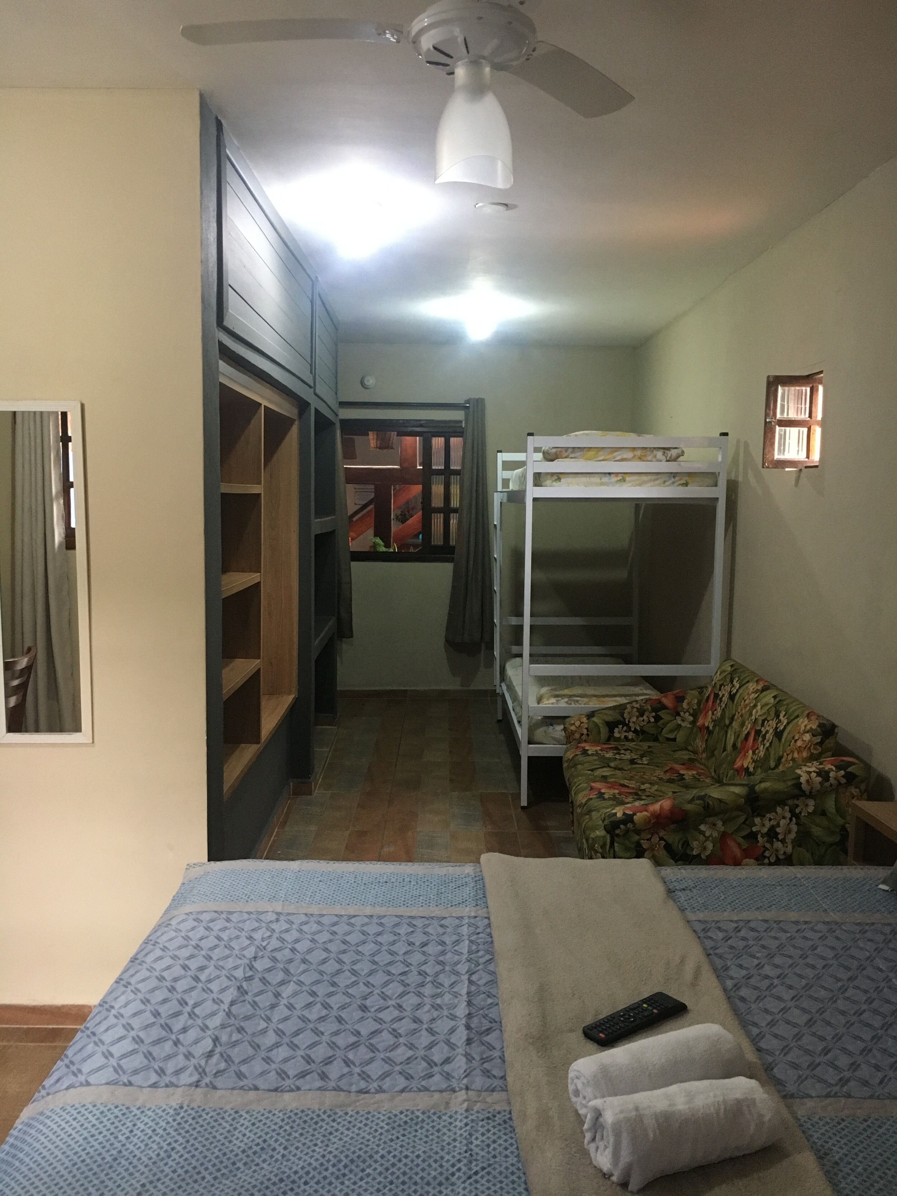 Quarto pequeno e compacto com uma cama de solteiro, um sofá e uma cama com roupa de cama estampada.