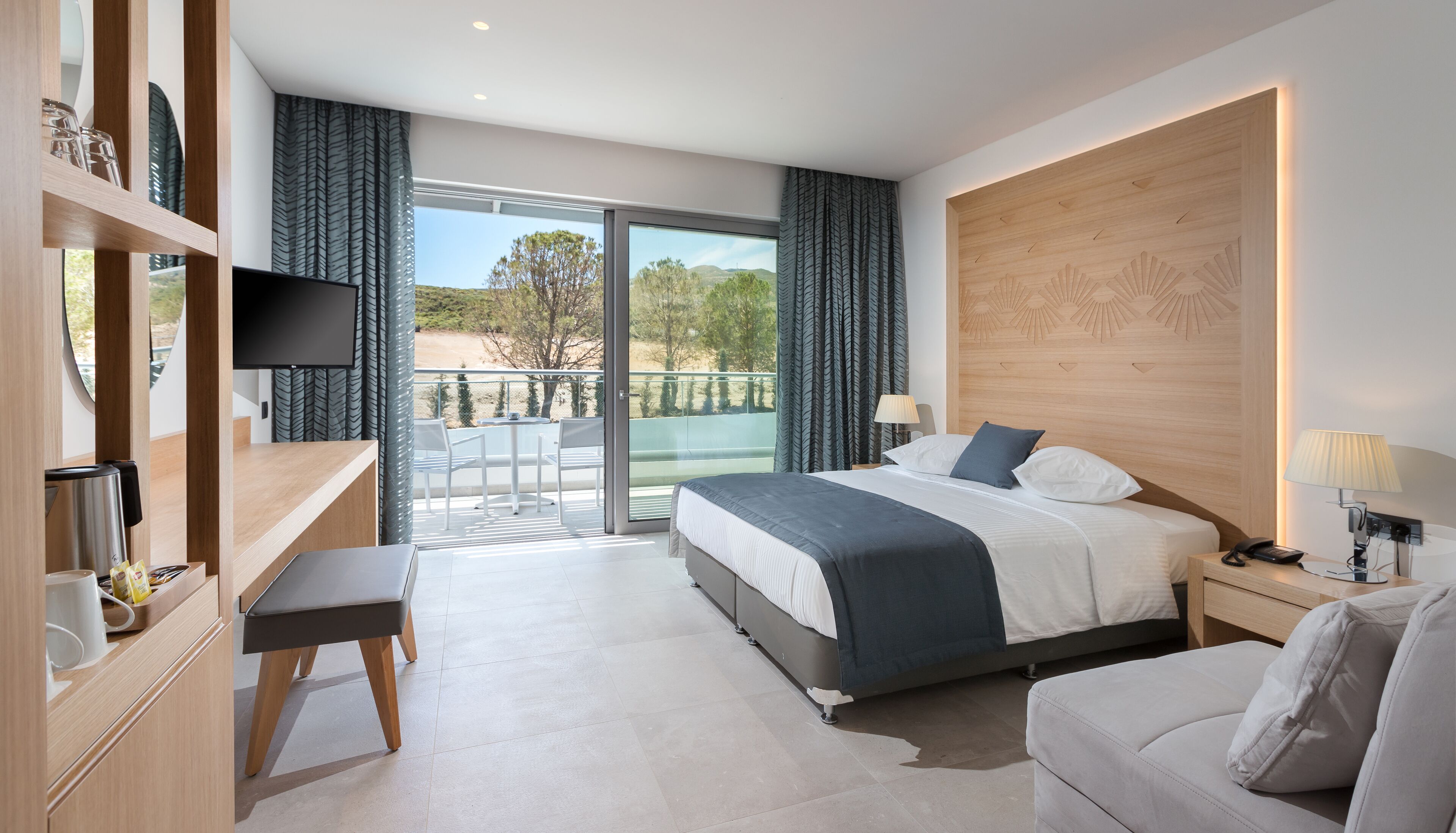 Quarto de hotel moderno com uma cama grande, uma mesa, uma cadeira e uma varanda com vista para o exterior.