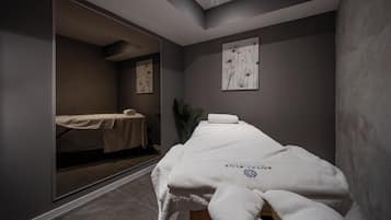Uma sala de spa moderna com uma mesa de massagem, um espaço de estar pequeno e um espelho.