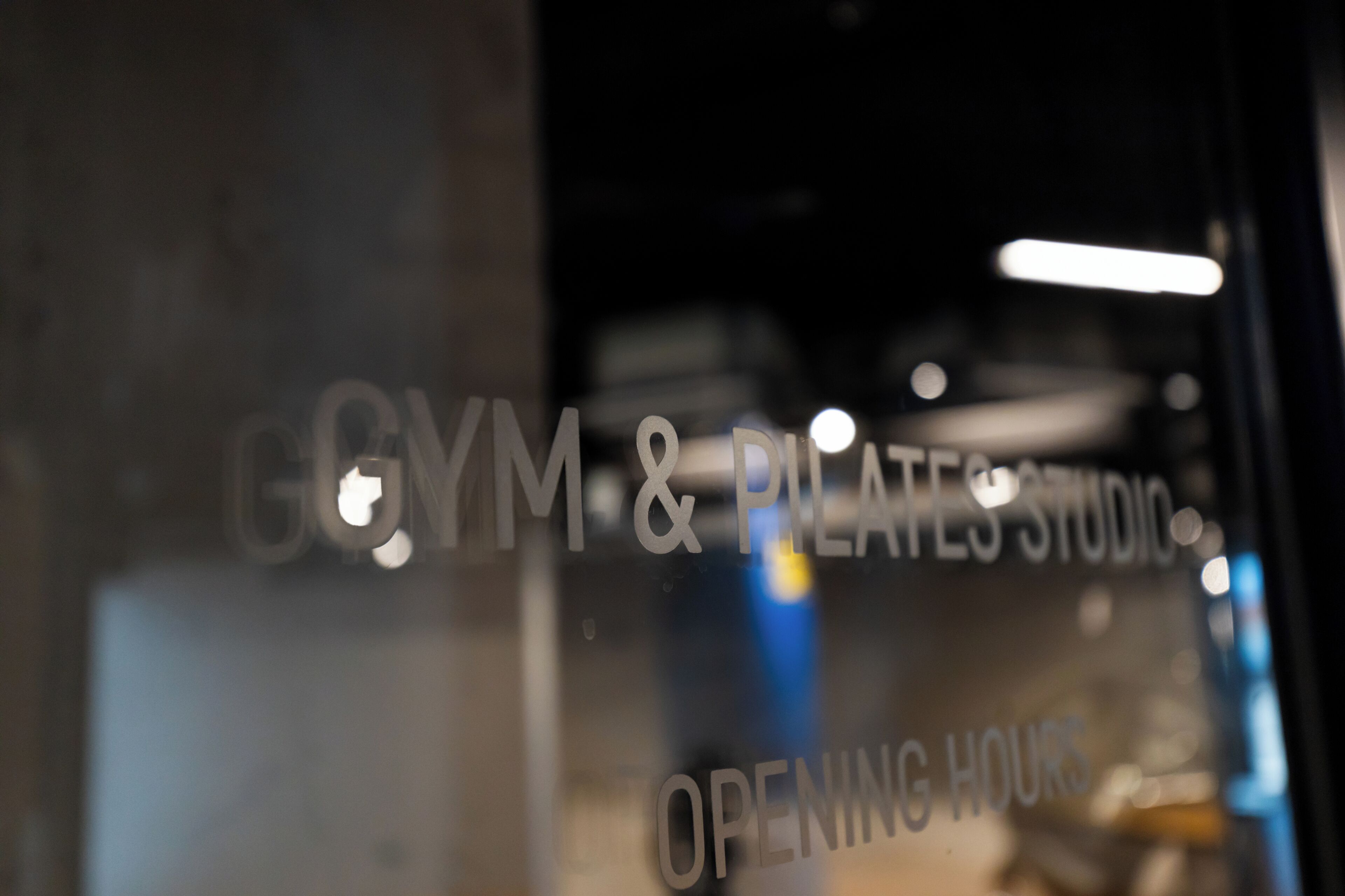 Placa com o texto 'GYM & Pilates Studio' e 'HORÁRIO DE FUNCIONAMENTO' numa janela de vidro.
