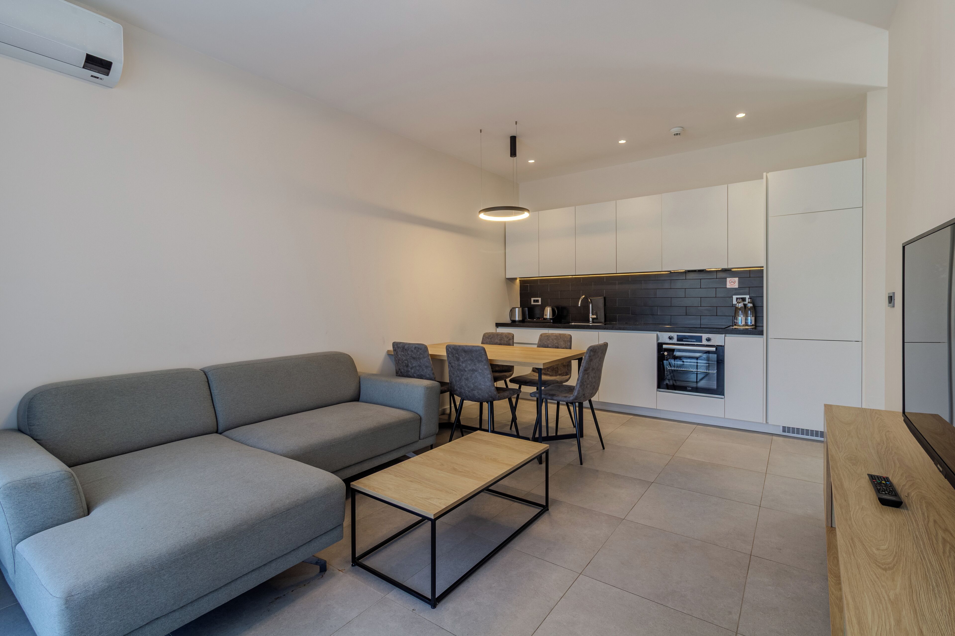 Uma sala de estar moderna com um sofá cinzento, uma mesa de centro de madeira e um espaço de jantar com uma mesa e cadeiras.