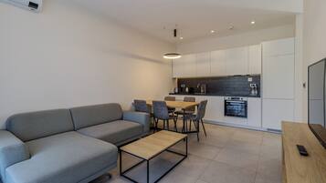 Uma sala de estar moderna com um sofá cinzento, uma mesa de centro de madeira e um espaço de jantar com uma mesa e cadeiras.