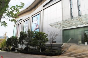 Um edifício moderno com entrada de vidro, degraus de acesso e um grande painel digital lateral.