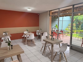 Interior de restaurante com várias mesas e cadeiras, vista para o exterior e uma parede de destaque vermelha.