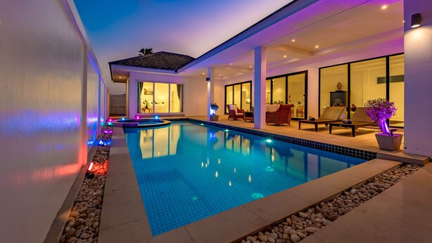 Piscina interior moderna com chão revestido, rodeada por uma área de descanso com cadeiras e uma planta em vaso.