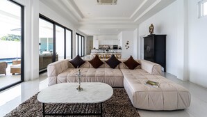 Uma sala moderna com um amplo sofá de canto, uma mesa de centro redonda e vista para a cozinha e área externa.