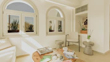 Um quarto bem iluminado com uma mesa de centro de madeira, um sofá branco e duas janelas em arco com plantas.