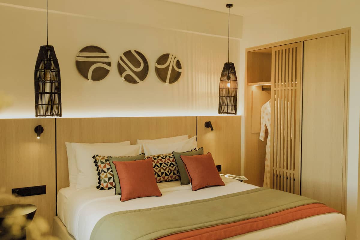 Quarto de hotel com cama, almofadas, mesa de cabeceira e guarda-roupa.