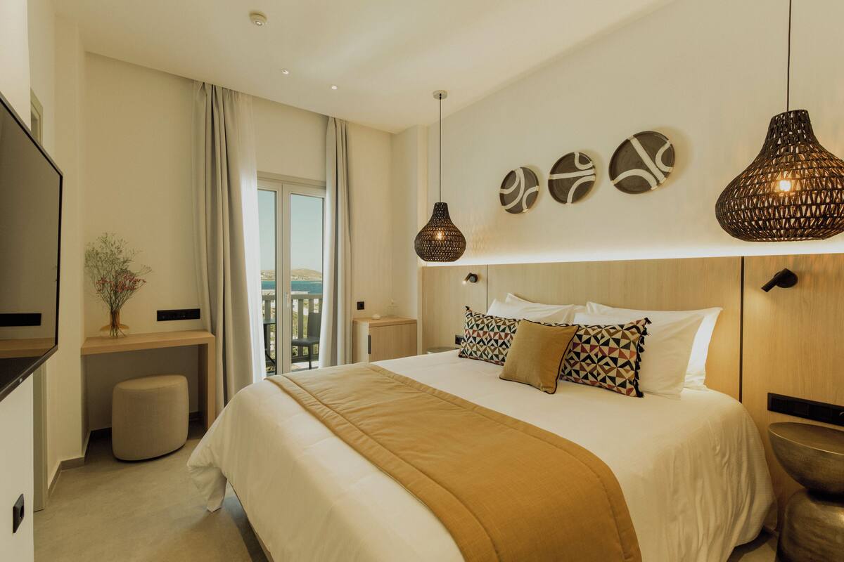 Quarto de hotel moderno com uma cama grande, uma escrivaninha e vista para o exterior.