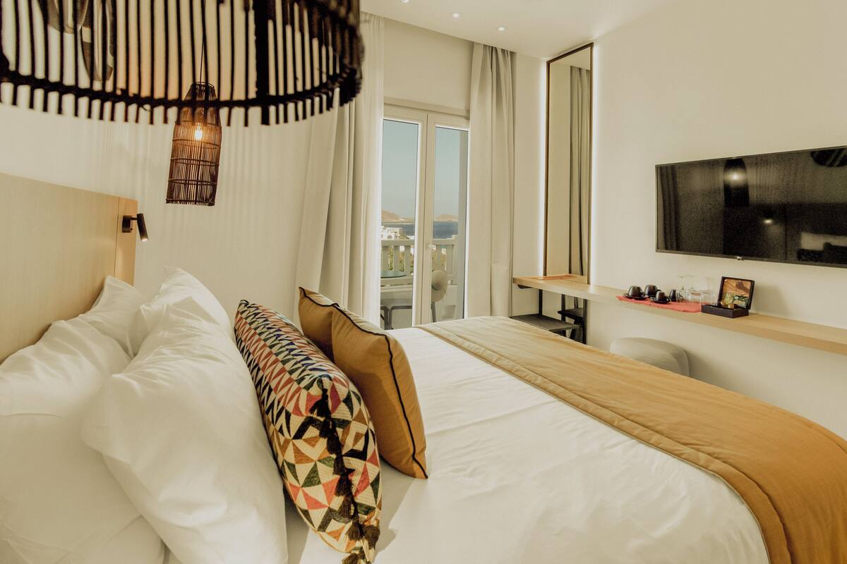 Quarto de hotel com cama grande, escrivaninha, televisão e vista para o mar.