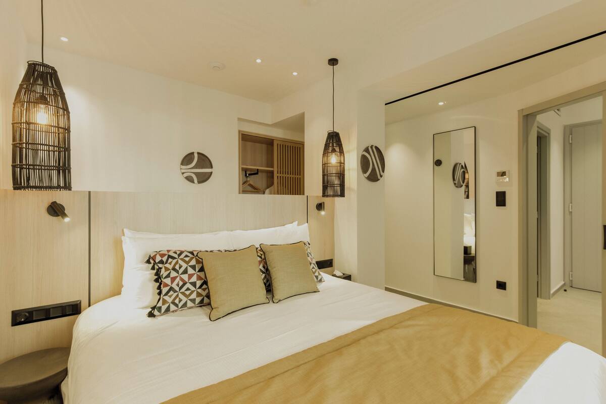 Quarto de hotel moderno com uma cama grande, um guarda-roupa, um espelho e iluminação pendente.