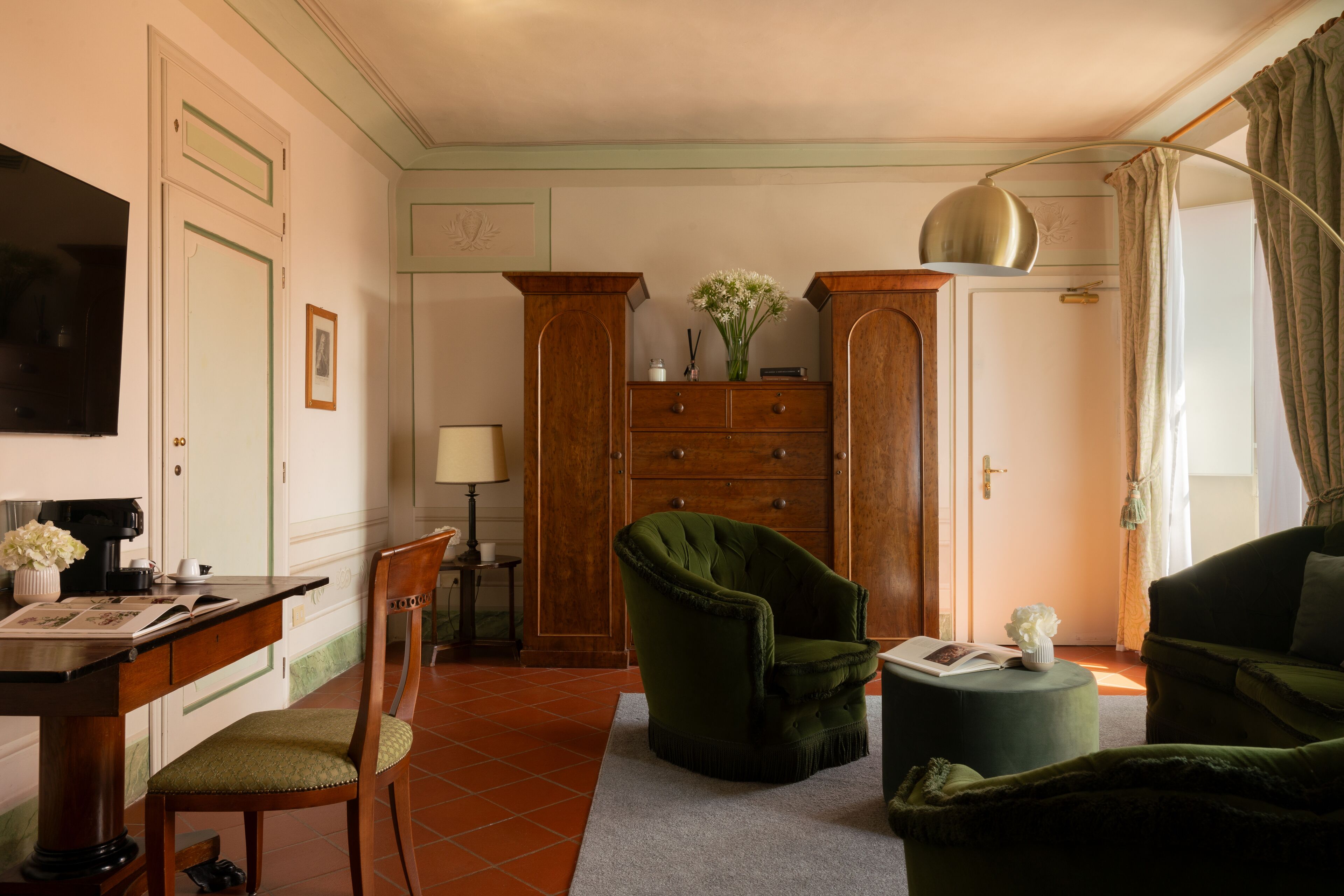 Uma sala de estar acolhedora com uma poltrona verde, um armário de madeira, uma televisão e uma luminária.