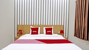 Quarto de hotel com cabeceira de madeira, duas almofadas vermelhas com o texto "OYO", manta com padrão vermelho e branco, e uma luminária vermelha no criado-mudo.
