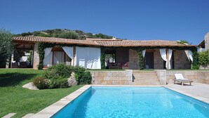 Uma casa de pedra de dois andares com piscina, cortinas brancas e um jardim.