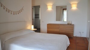 Quarto com cama, cómoda de madeira, espelho e luminárias na parede.