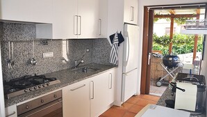 Cozinha compacta com armários brancos, bancada de granito, fogão a gás, pia e geladeira.