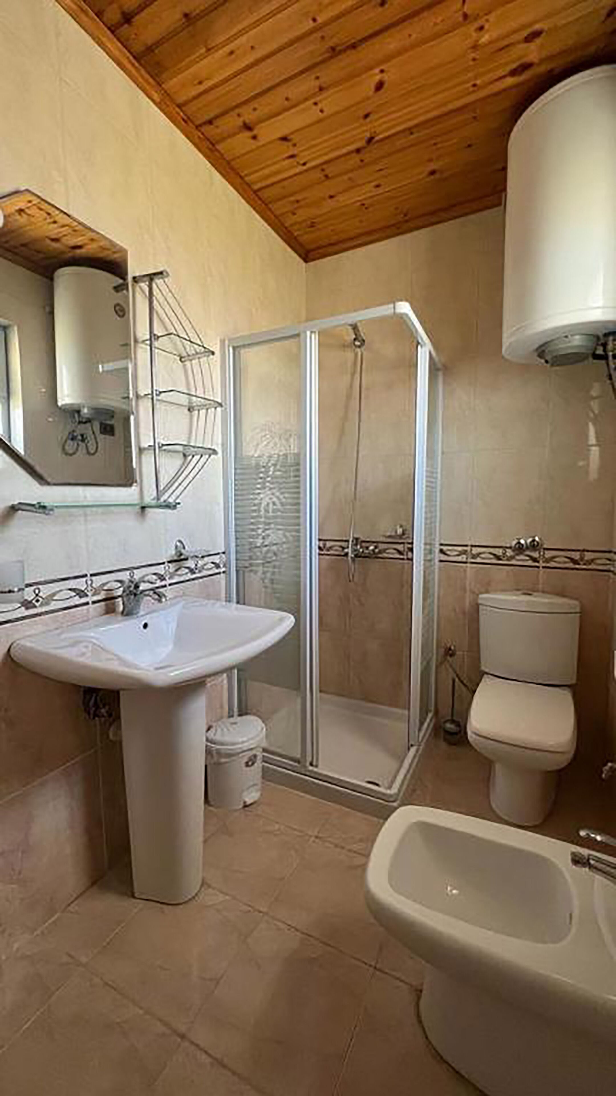 Casa de banho com lavatório de pedestal, chuveiro com proteção de vidro, sanita e bidé.